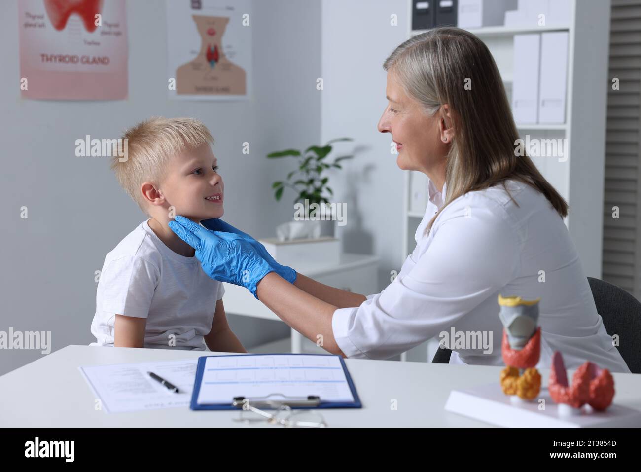 Endocrinologist examining boy's thyroid gland at table in hospital ...