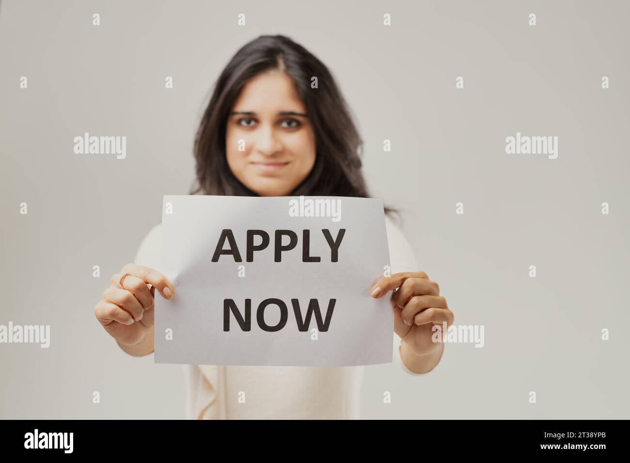 Holding a 'APPLY NOW' sign, the woman's gaze captures a mix of hope and ...