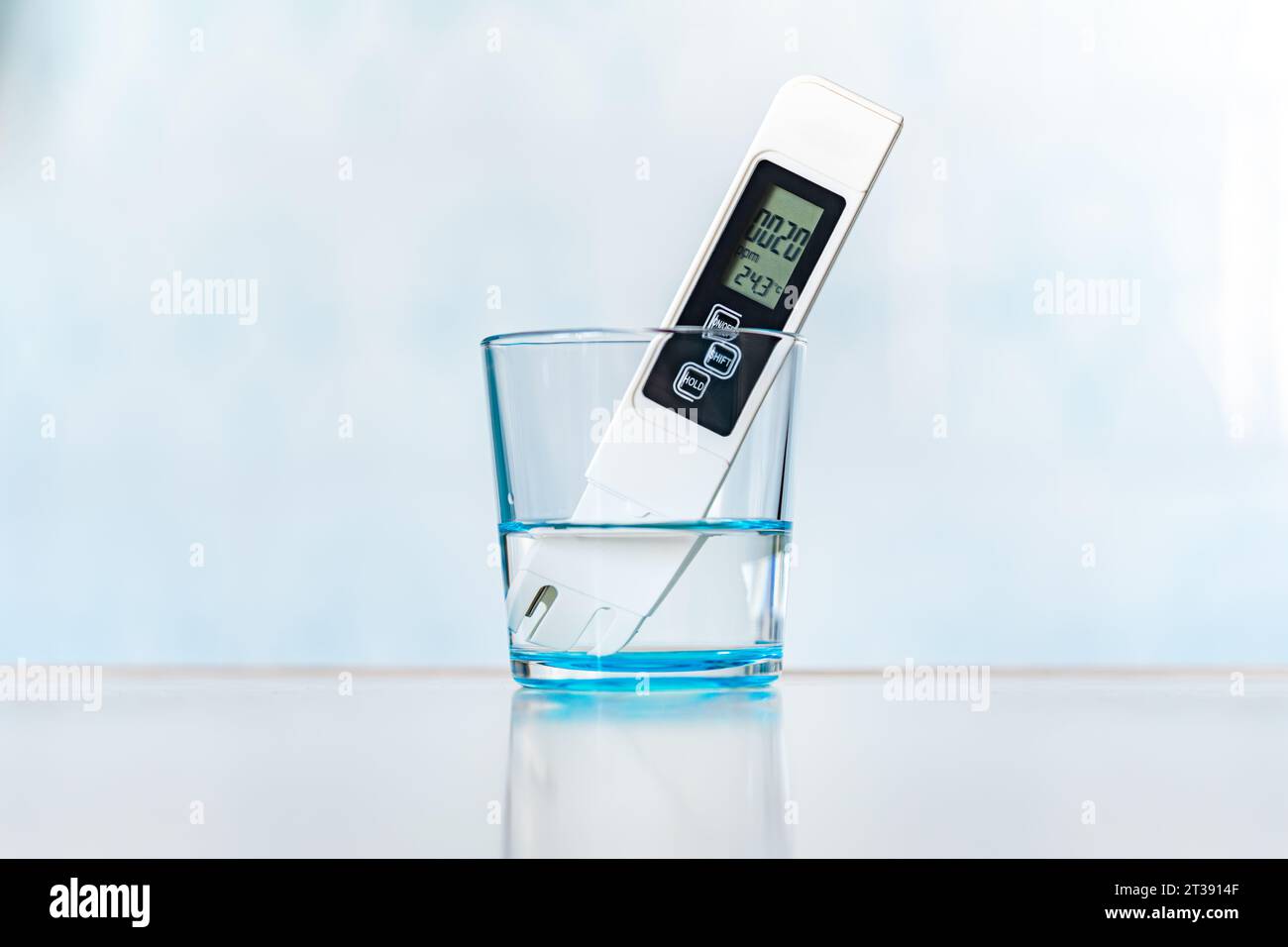 Water quality meter tester submerged in drinking glass, on blue ...