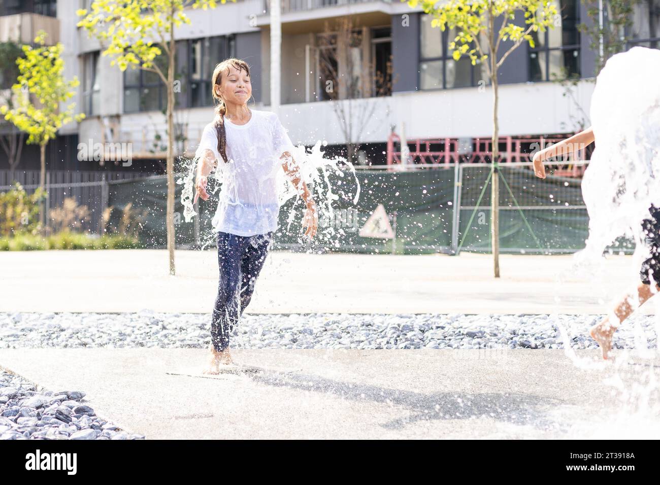 Cheerful young teen girl in city fountain, girl in wet clothes is ...