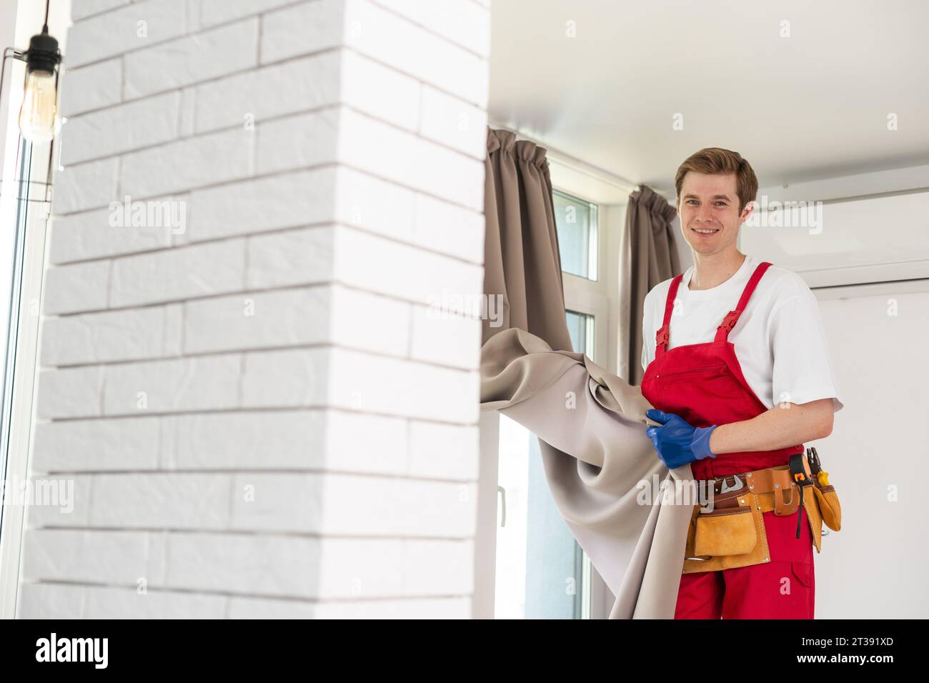 A male repairman installs a curtain rod and hangs curtains in the house ...