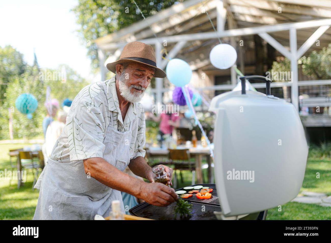Senior man grilling at bbq garden party. Elderly chef using herbs to ...