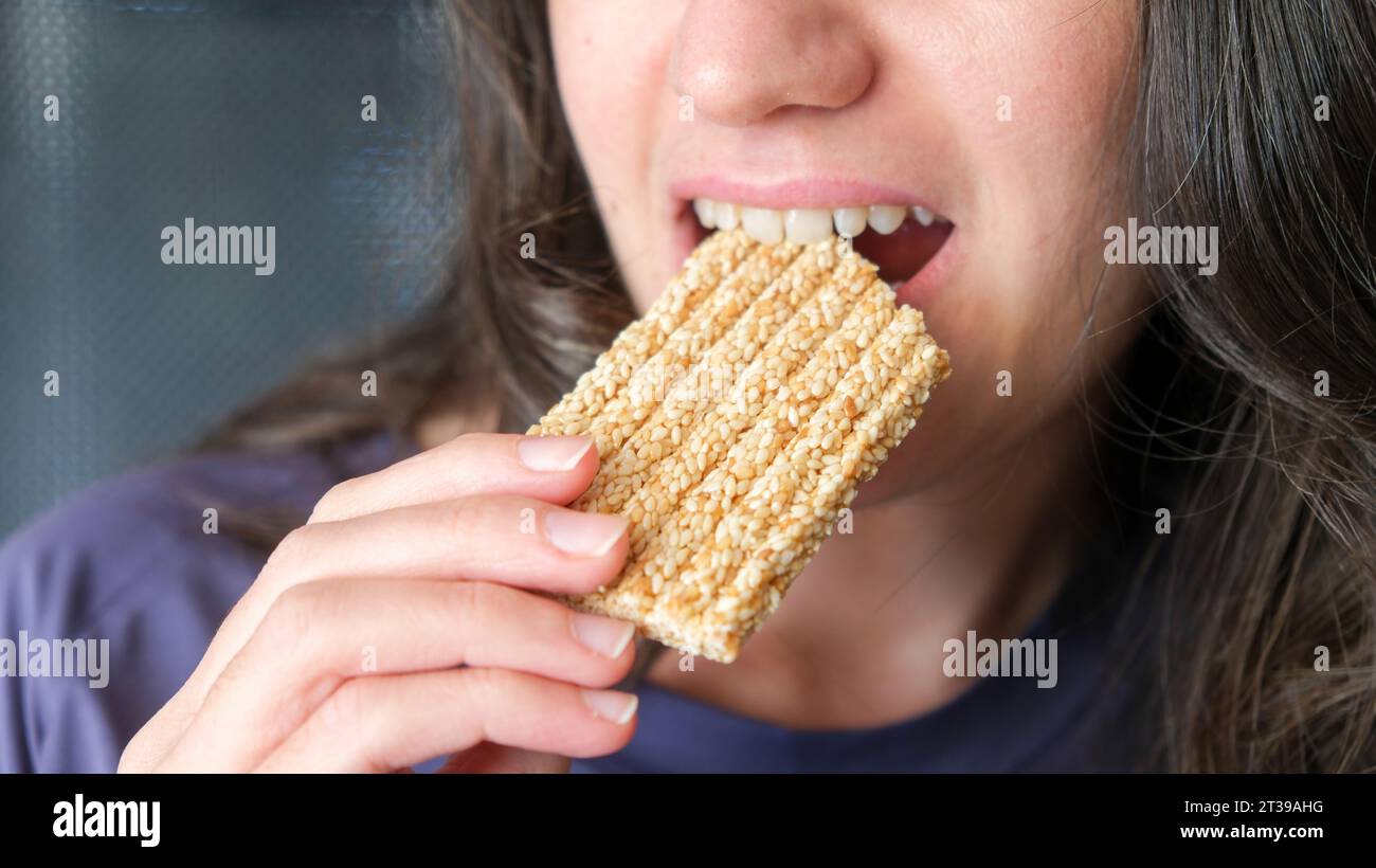 A young female is enjoying a snack while holding an object in her hands ...