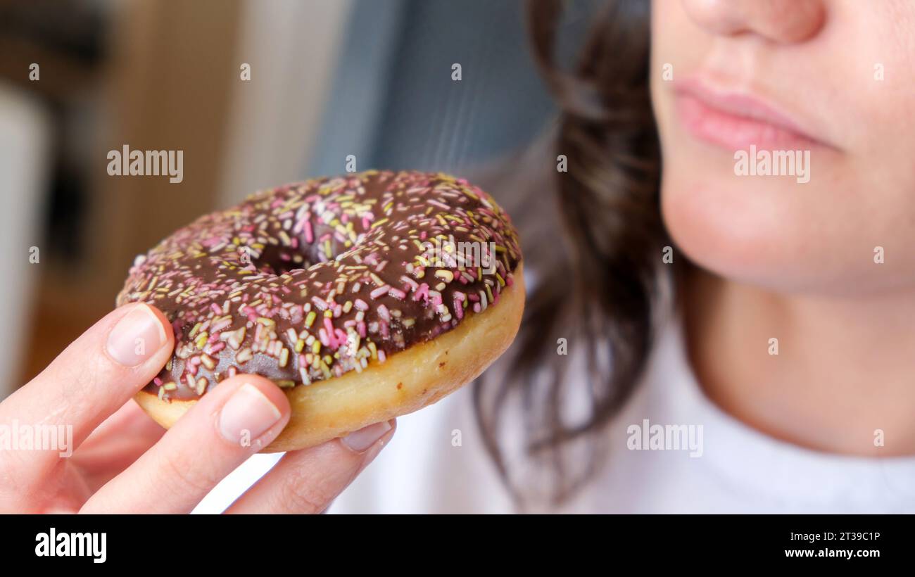 A young female adult is smilingly displaying a freshly-baked doughnut ...
