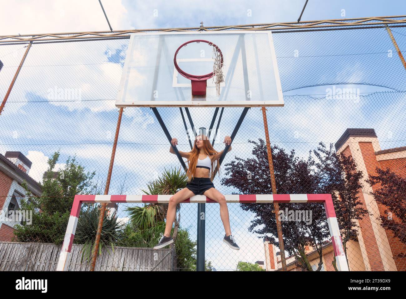 Young redhead woman over soccer goal and hanging on a basketball ring ...