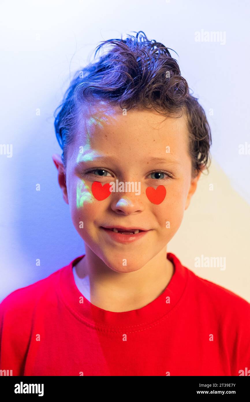A young boy with curly hair and heart-shaped stickers on his cheeks ...