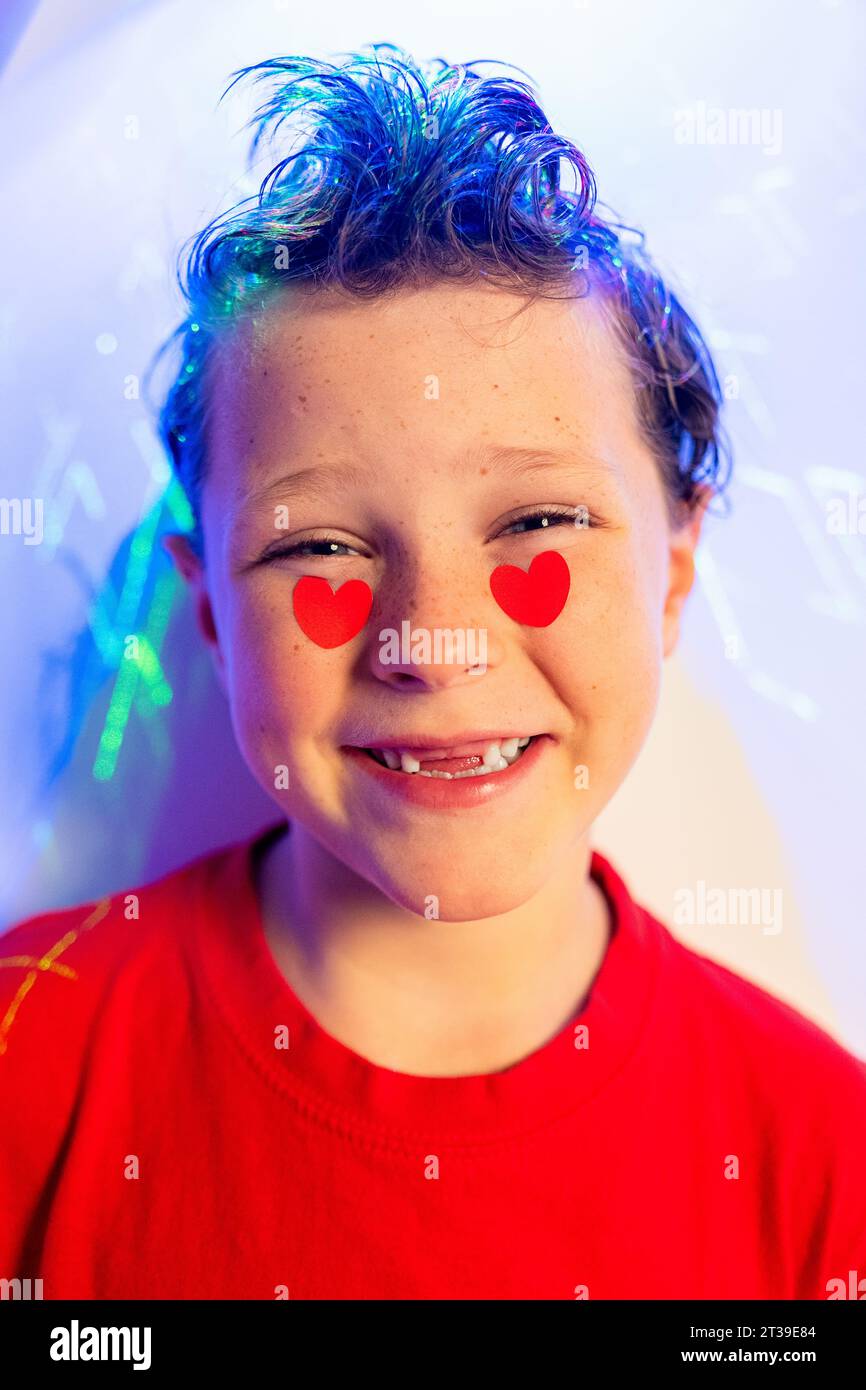 A young boy with curly hair and heart-shaped stickers on his cheeks ...
