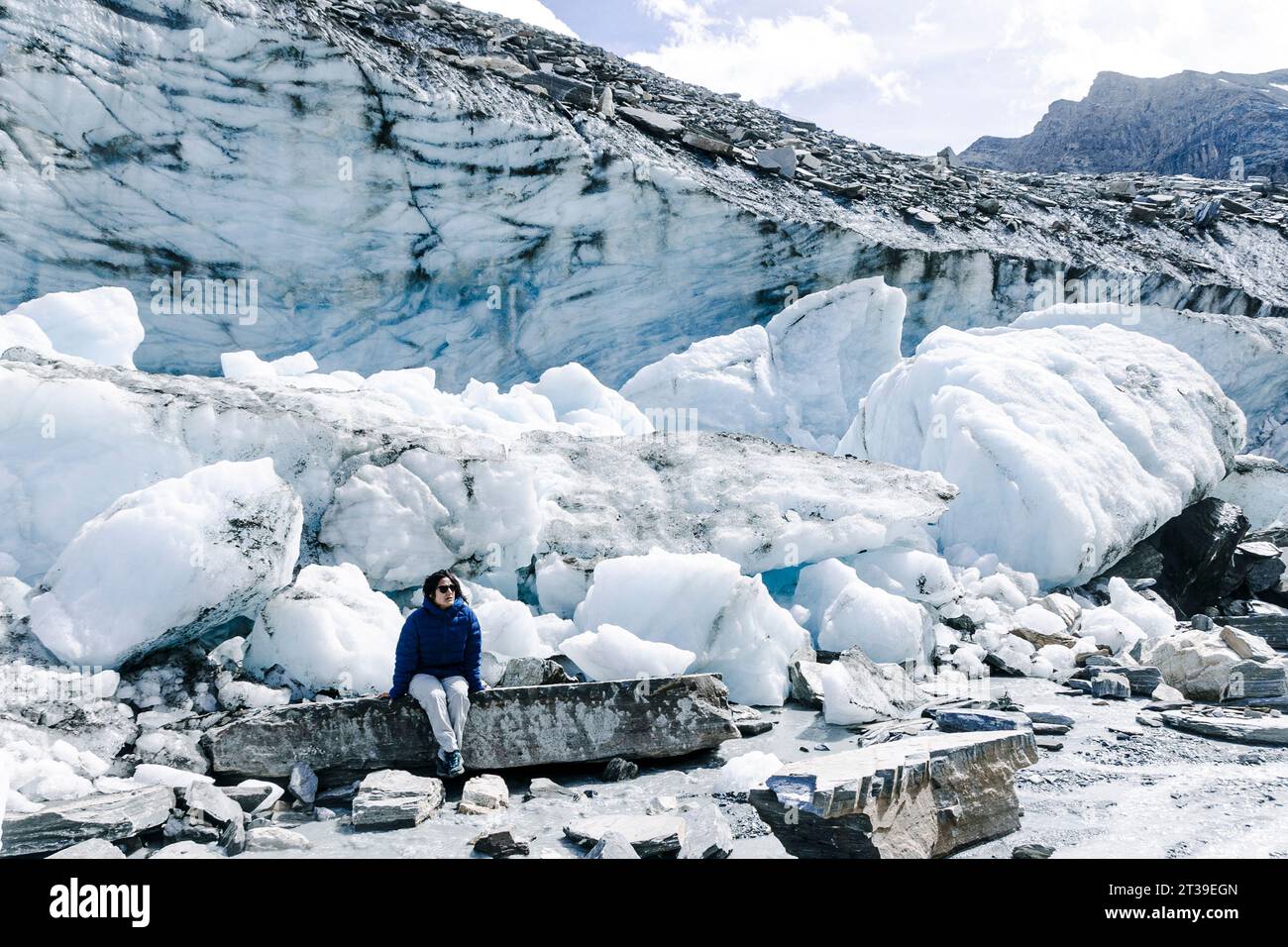 An individual in a blue jacket sits on a large rock amid a breathtaking ...