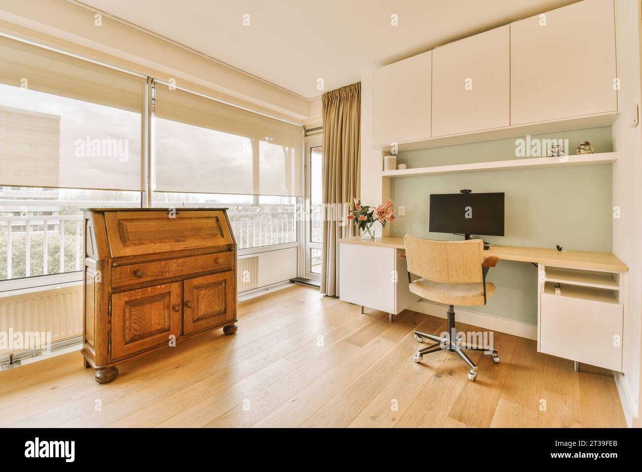 Computer on desk with empty chair and wooden dresser by large window in ...