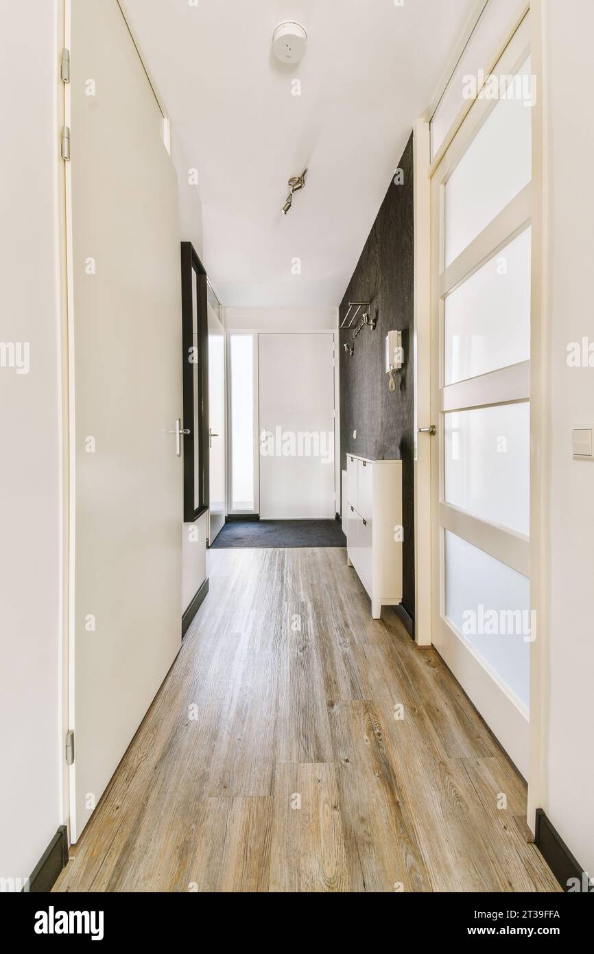 Long empty hallway with white closed doors and black wall with hooks in ...