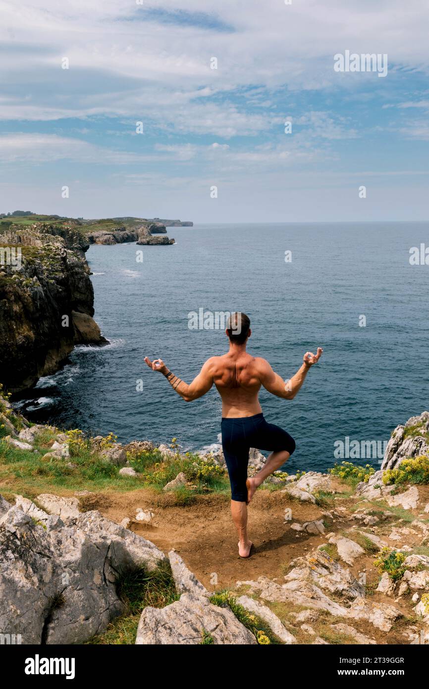 Mature man practicing yoga with a tranquil ocean backdrop, balancing on ...