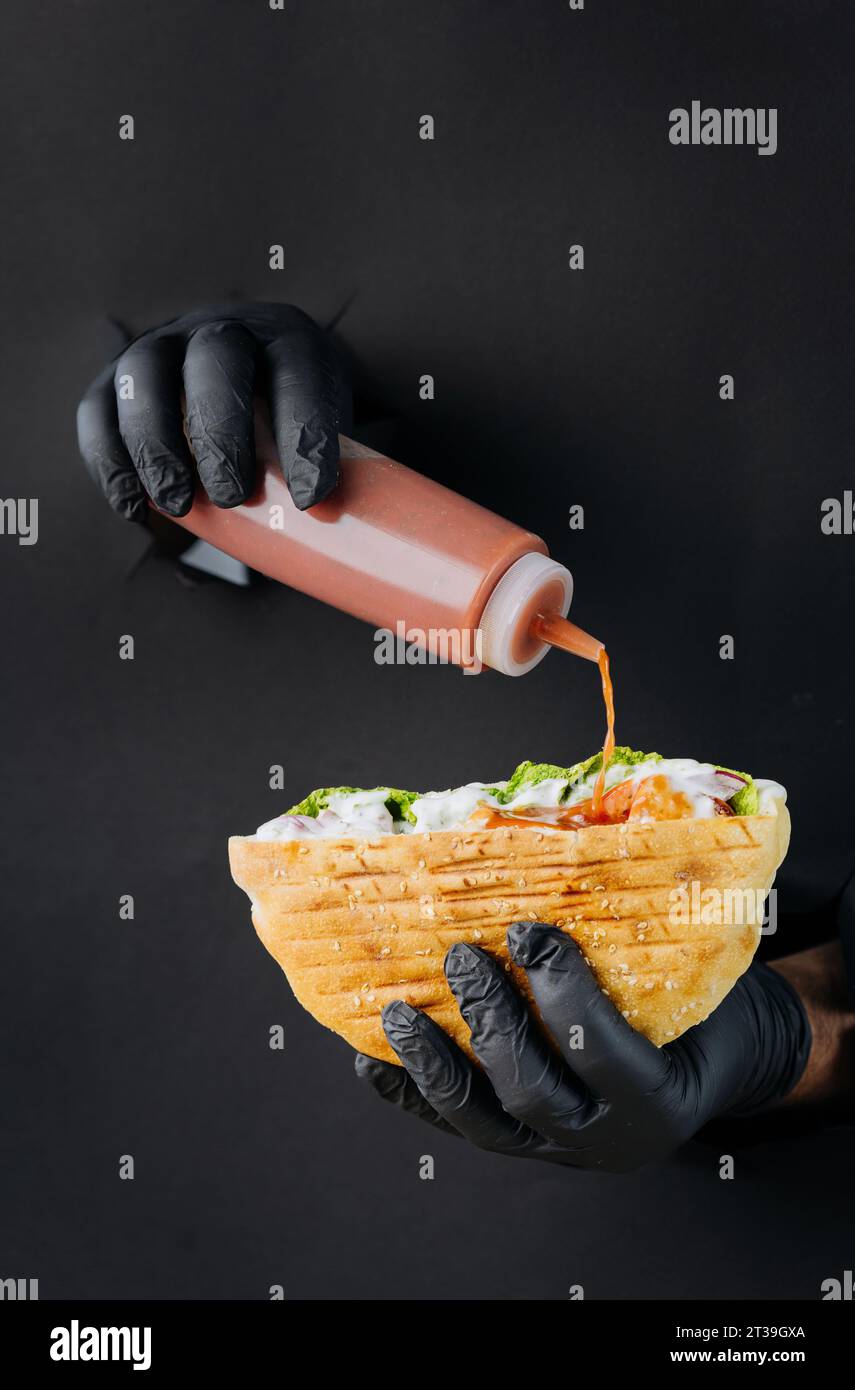 Cooks hand adding sauce to doner kebab through torn holes on black ...