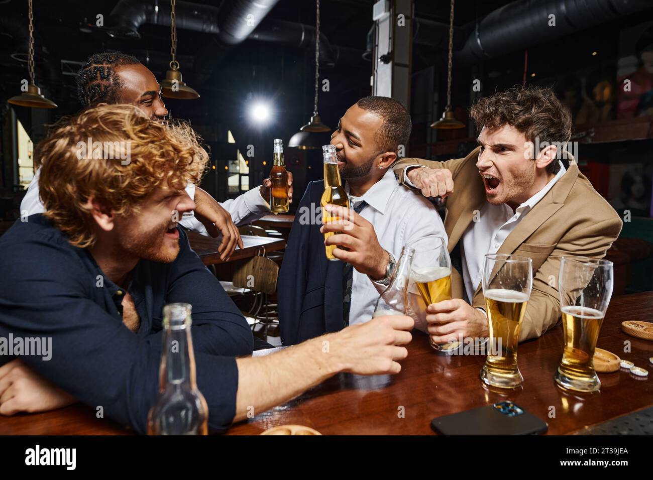 emotional and interracial colleagues in formal wear drinking beer in ...