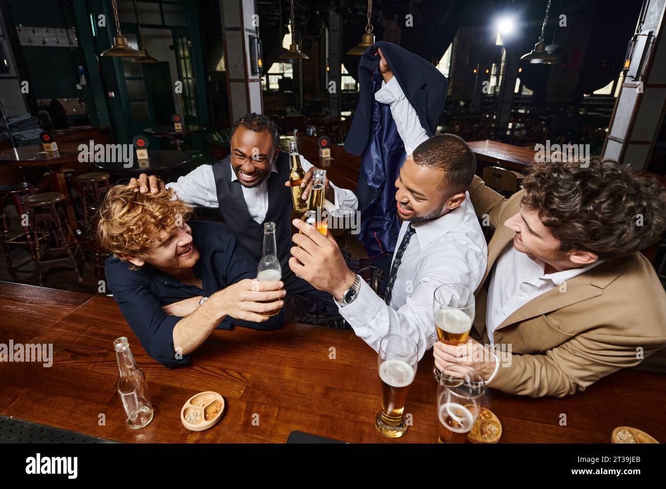 group of four happy colleagues in formal wear joking and drinking beer ...