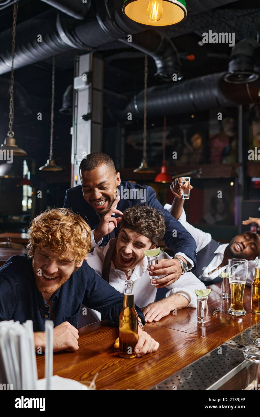 drunk and funny interracial men in formal wear laughing while drinking ...