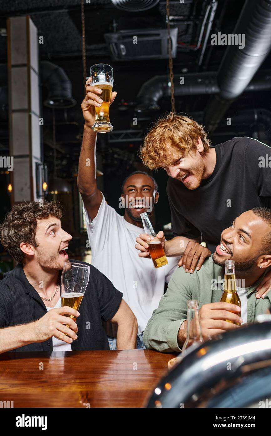 excited african american man raising glass of beer near cheerful ...