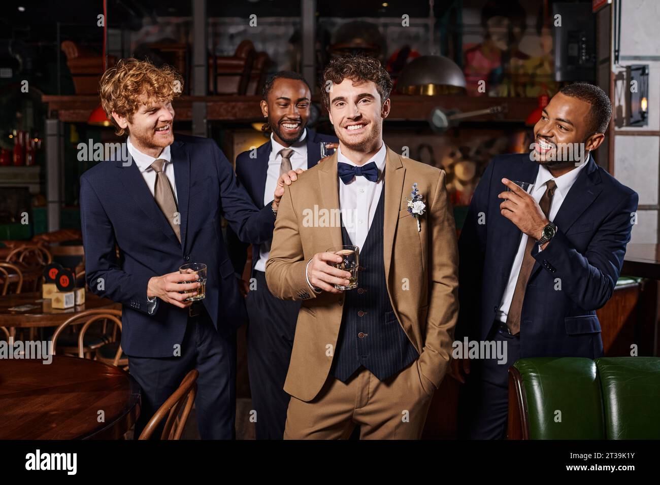 bachelor party, happy interracial best men looking at groom in suit ...
