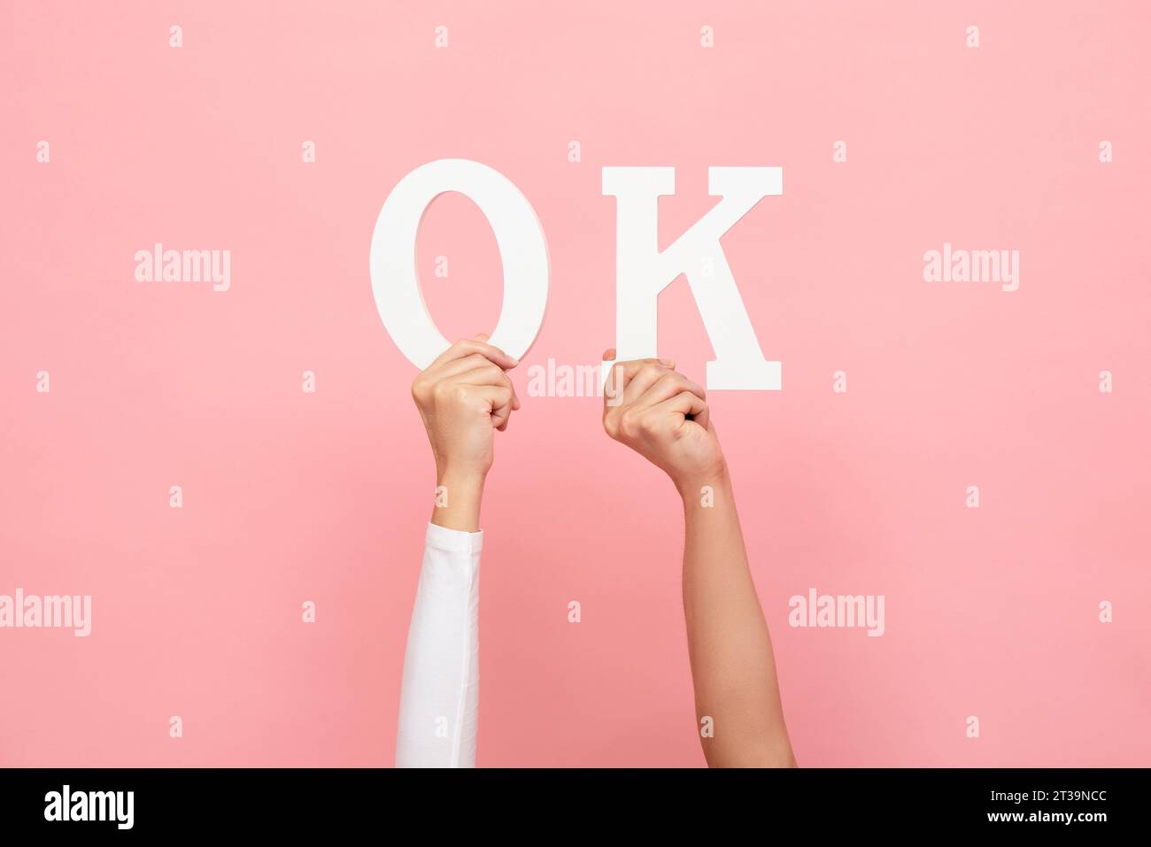 OK letter sign being raised by two hands in pink isolated studio ...