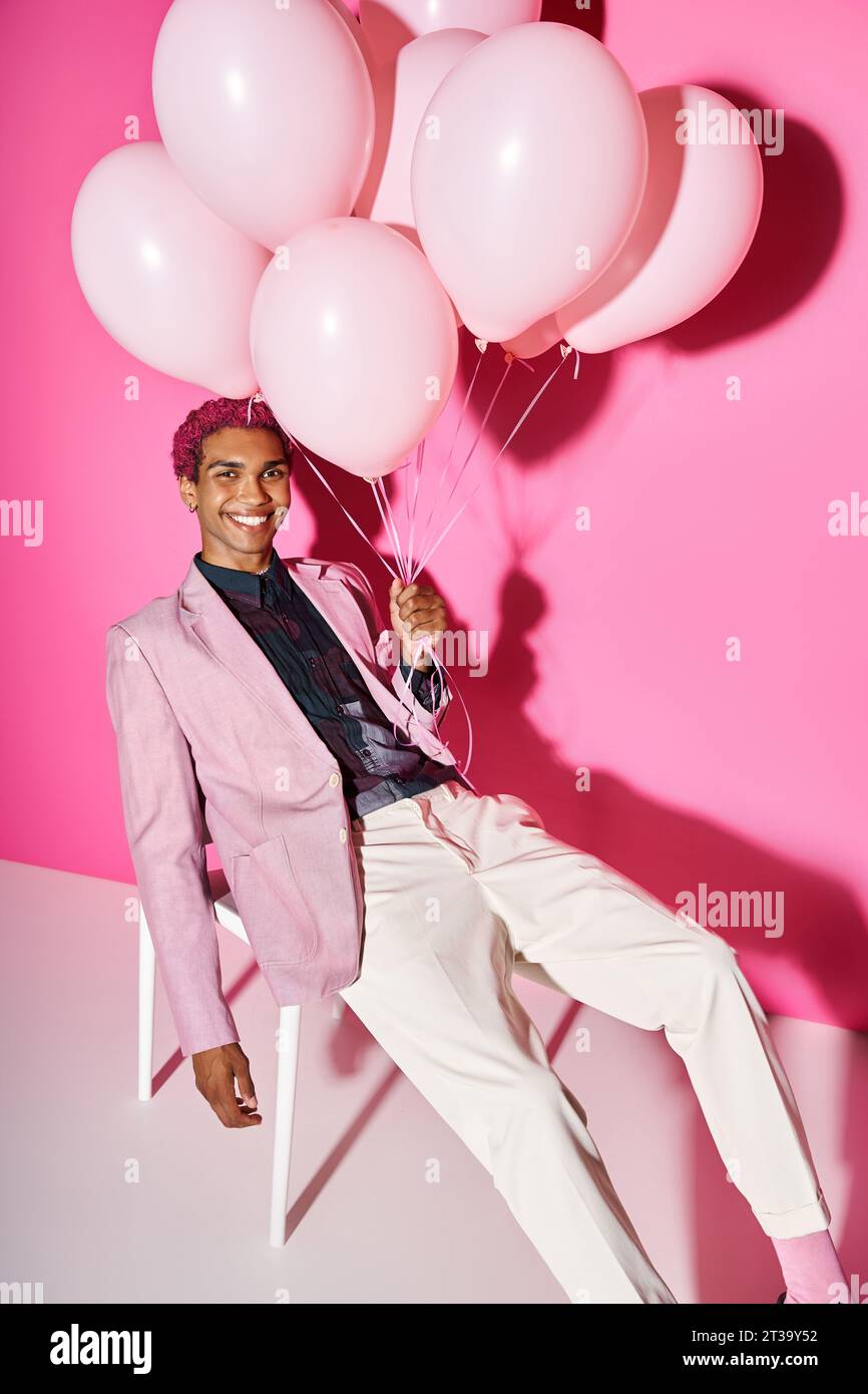 joyous man sitting unnaturally on white chair with balloons and smiling ...
