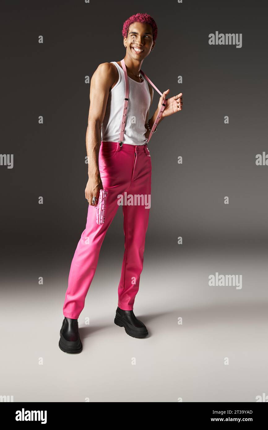 cheerful young man in pink attire winking and smiling holding pink toy ...