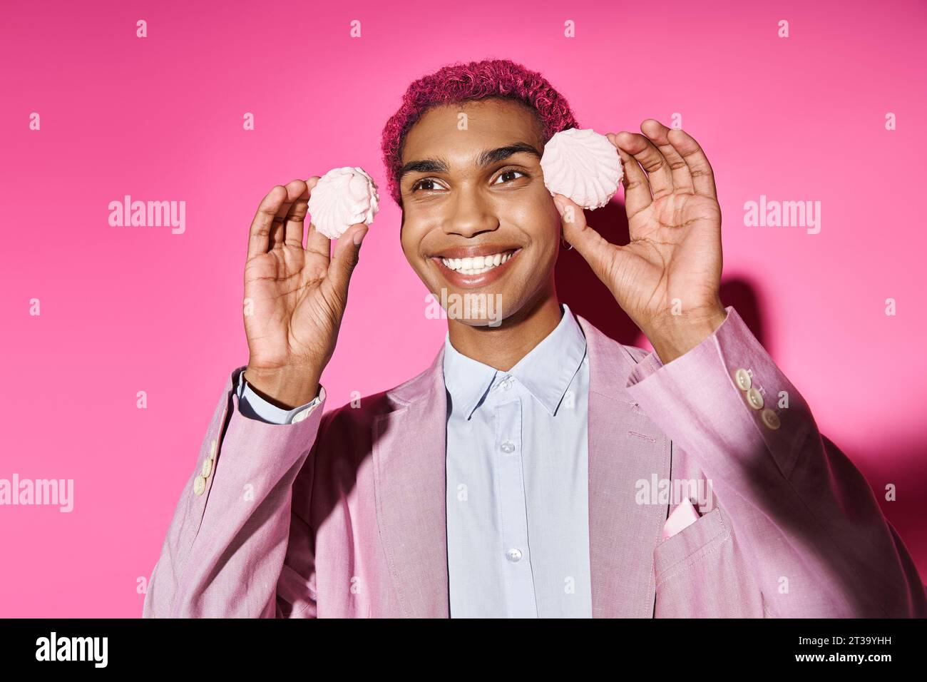 cheerful man posing with delicious pink zefir near face on pink ...