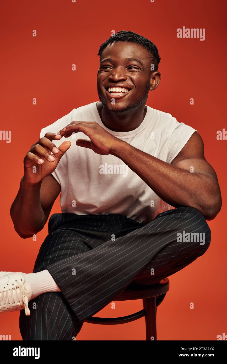 laughing african american man in white tank top sitting on chair and ...
