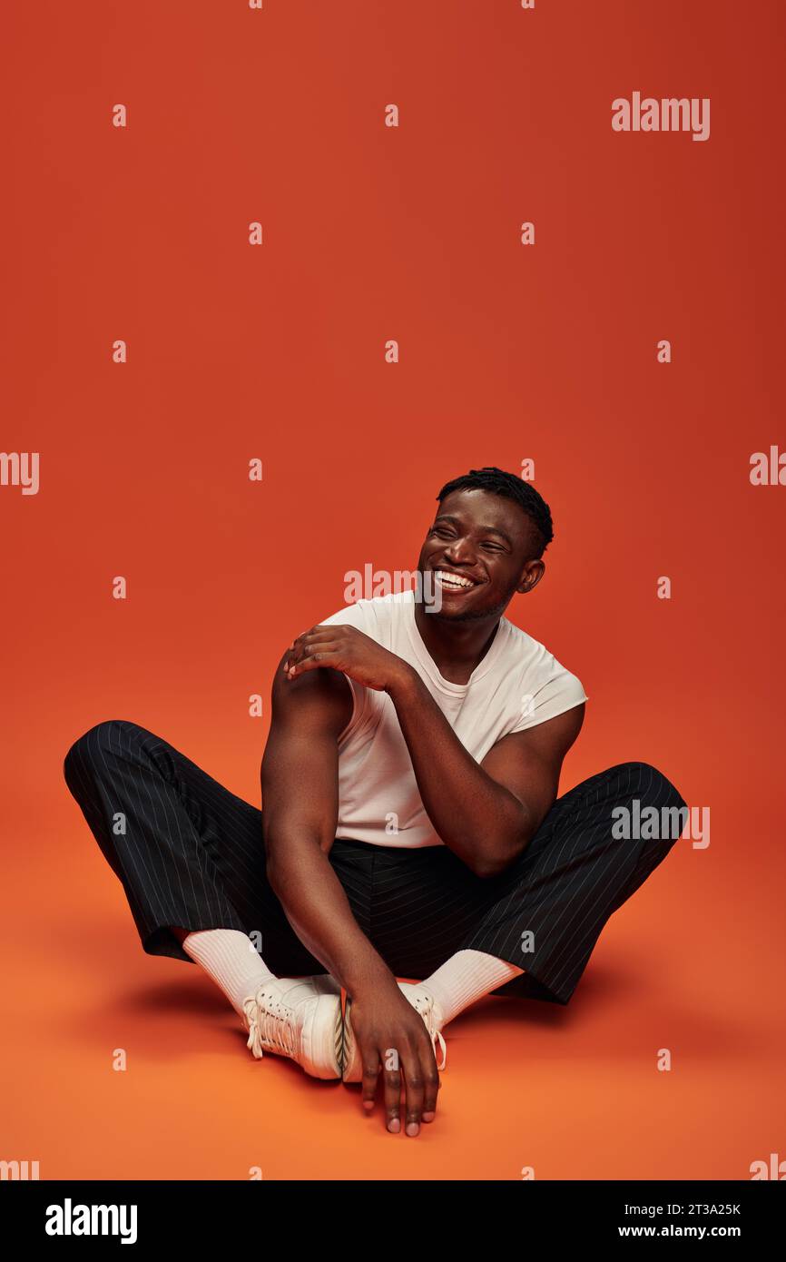 excited stylish african american man sitting and laughing with closed ...