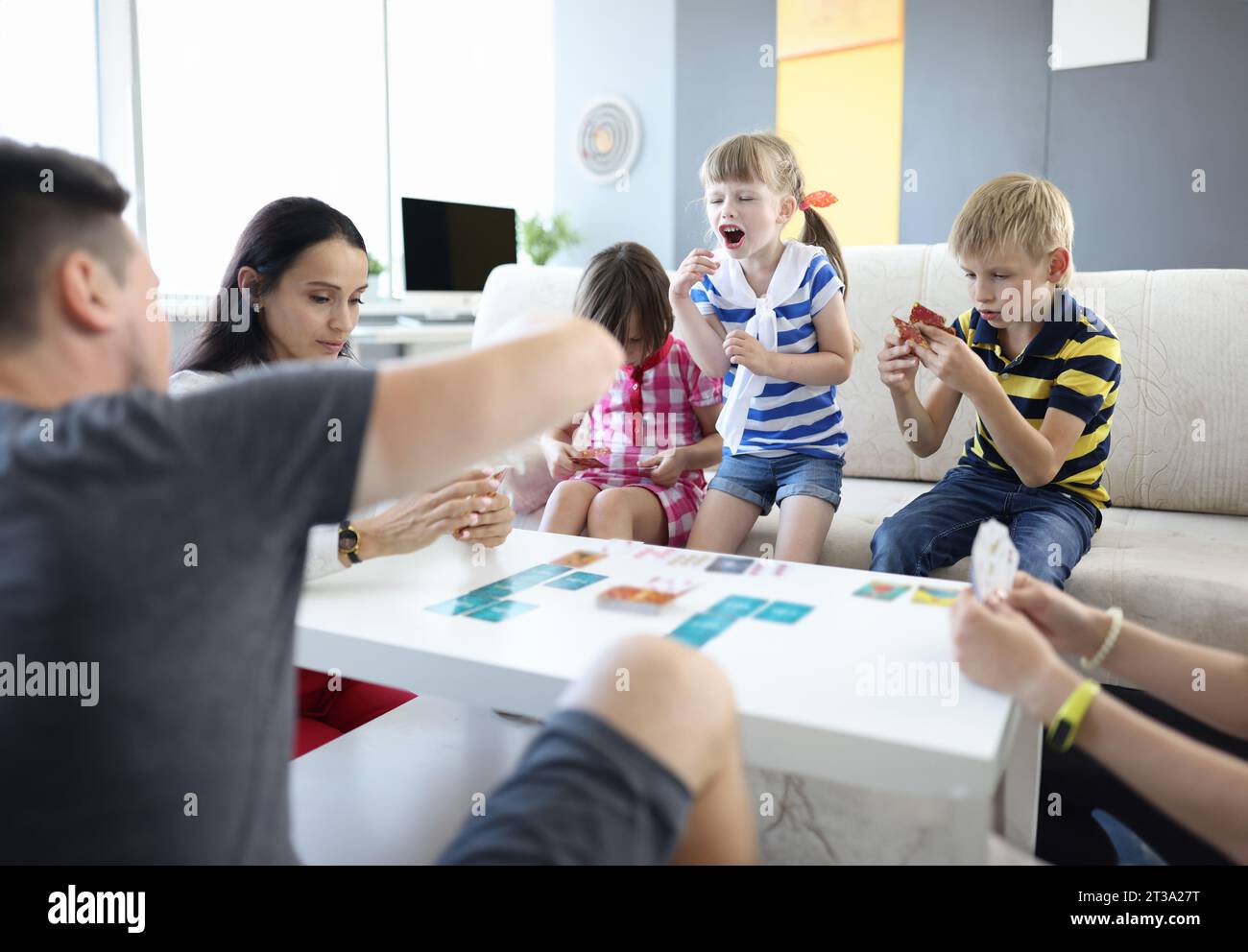 Adults and children are sitting at table and holding playing cards girl ...