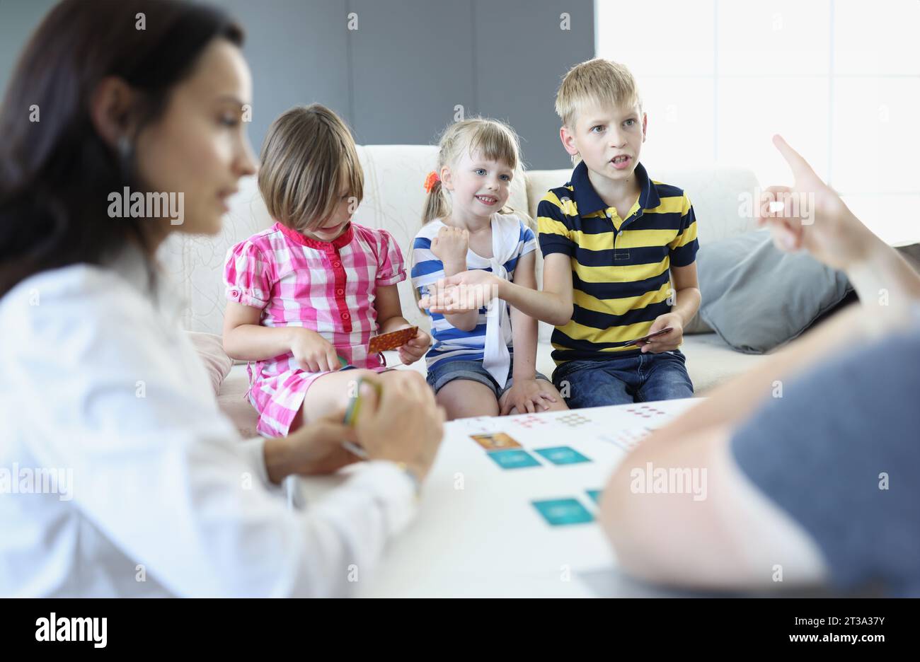 Adults and children sit around a table on which playing cards are ...