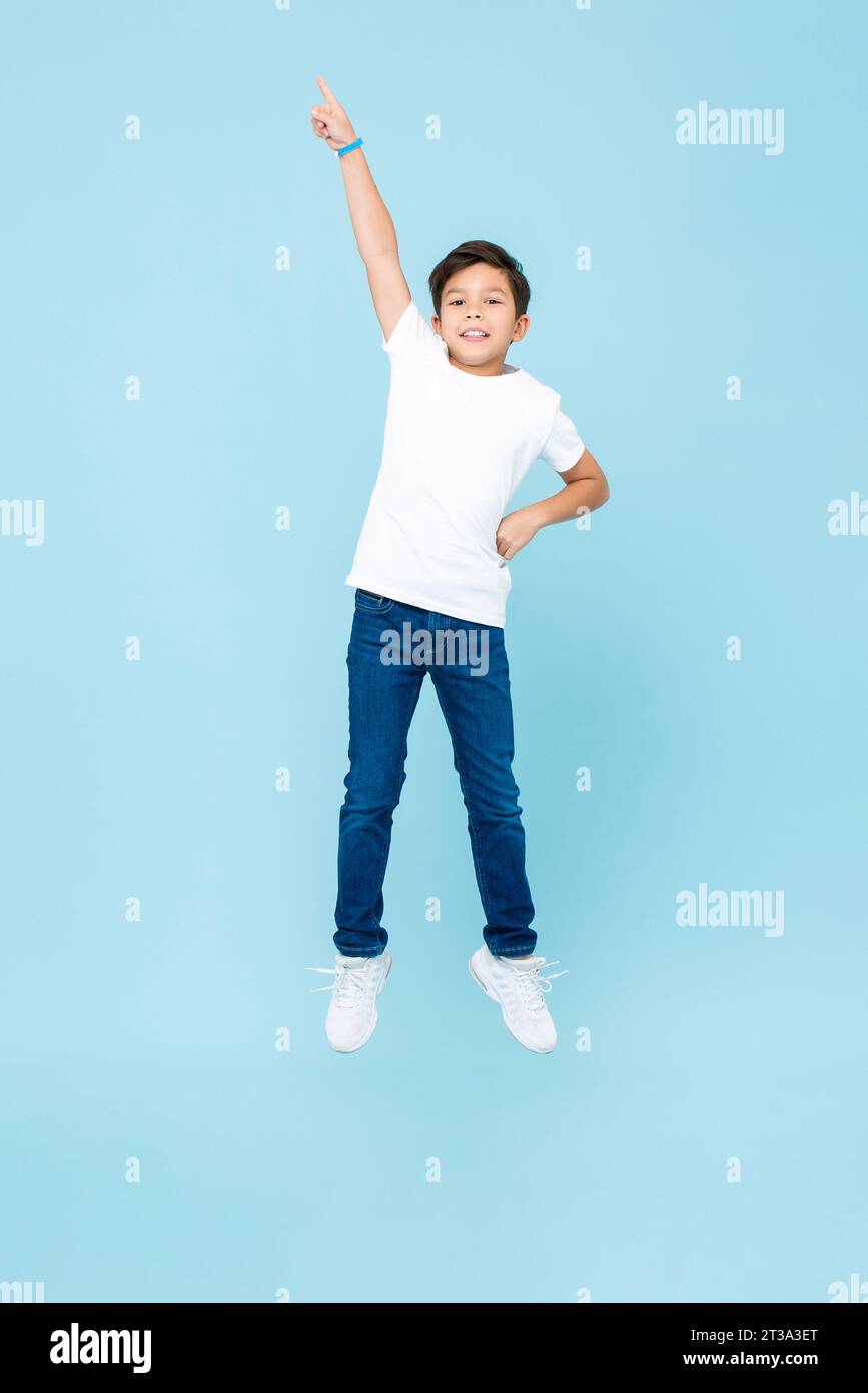 Young mixed race Asian kid boy jumping with hand pointing up in the air ...
