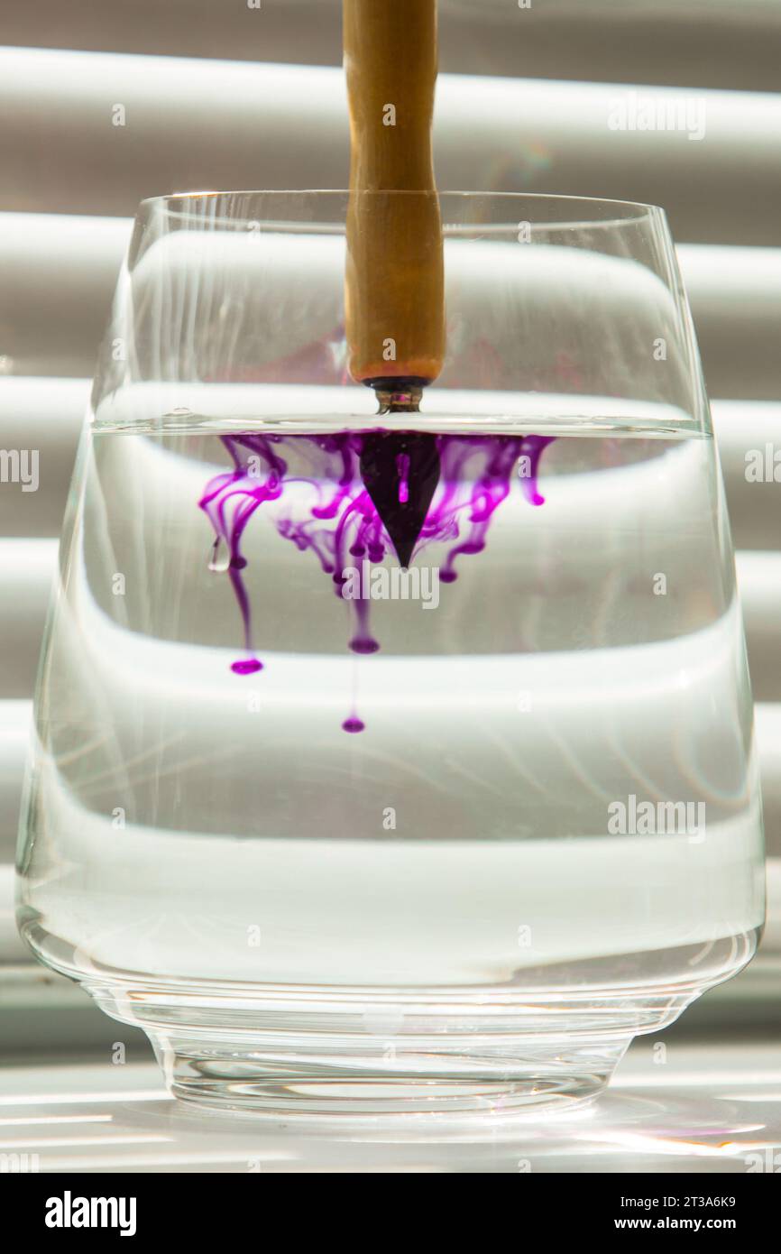 metal tip of ink pen dipped in water. diffusion of blue ink in a ...
