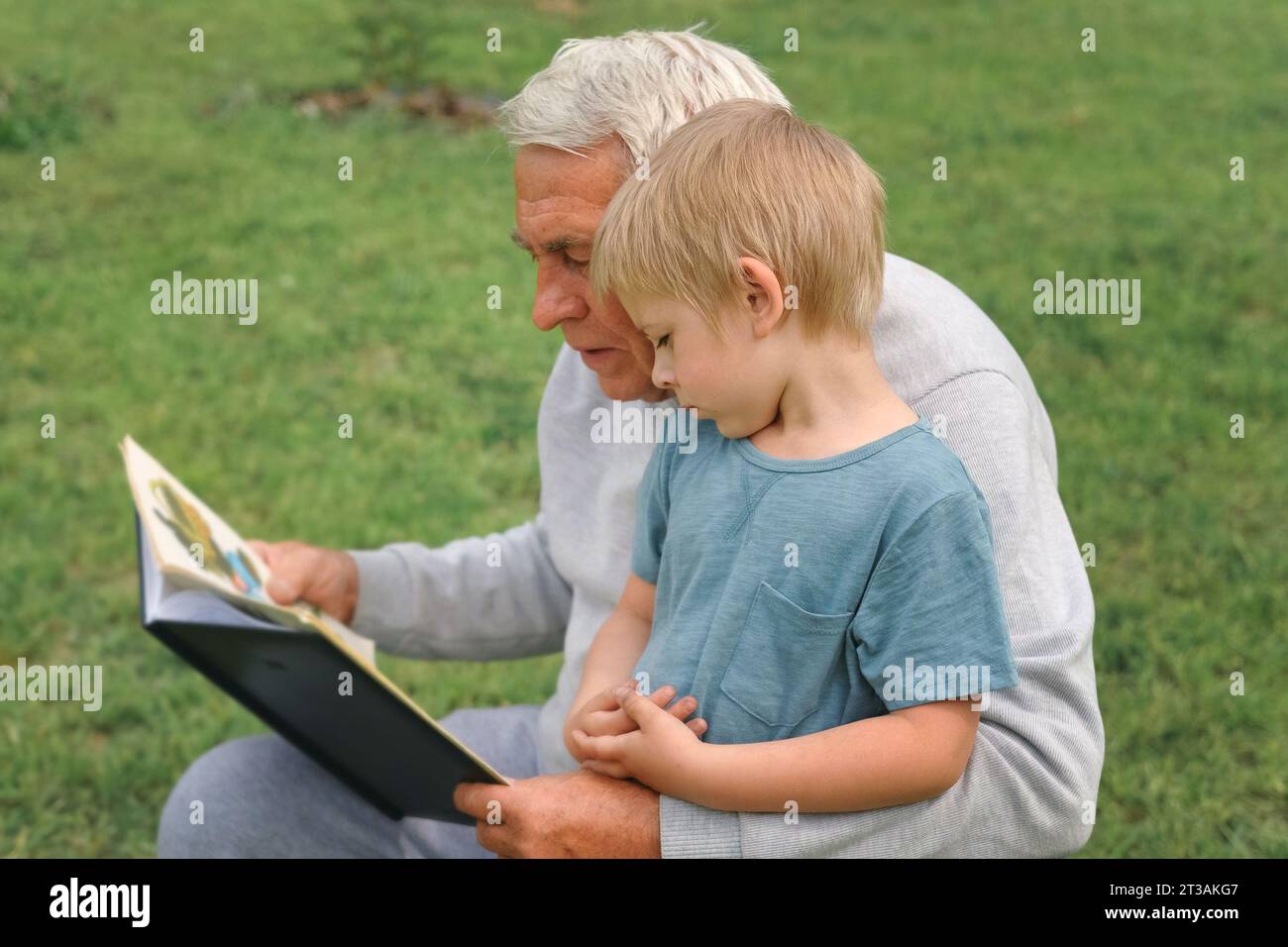 Happy grandfather reading book to curious grandson outdoors. Close up ...