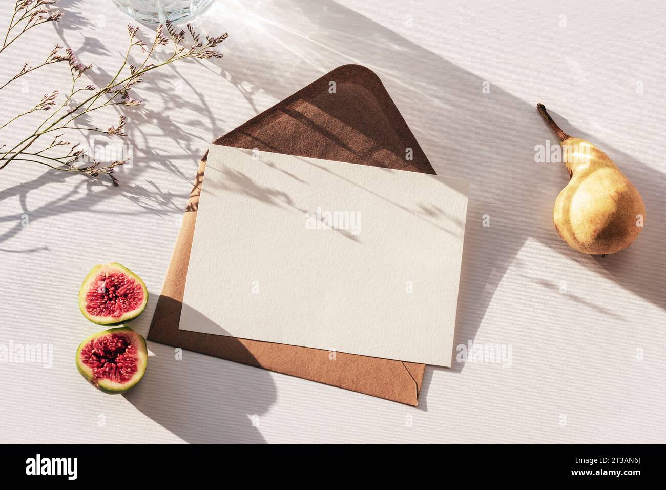 Envelope with blank card, glass of water, pear, figs and flowers in ...