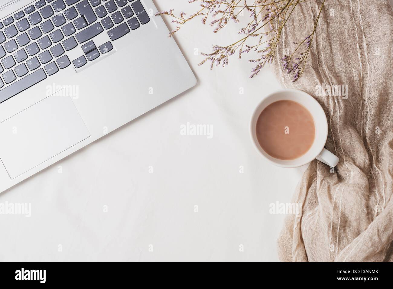 Coffee cup, laptop computer and small kermek flowers on white linen ...
