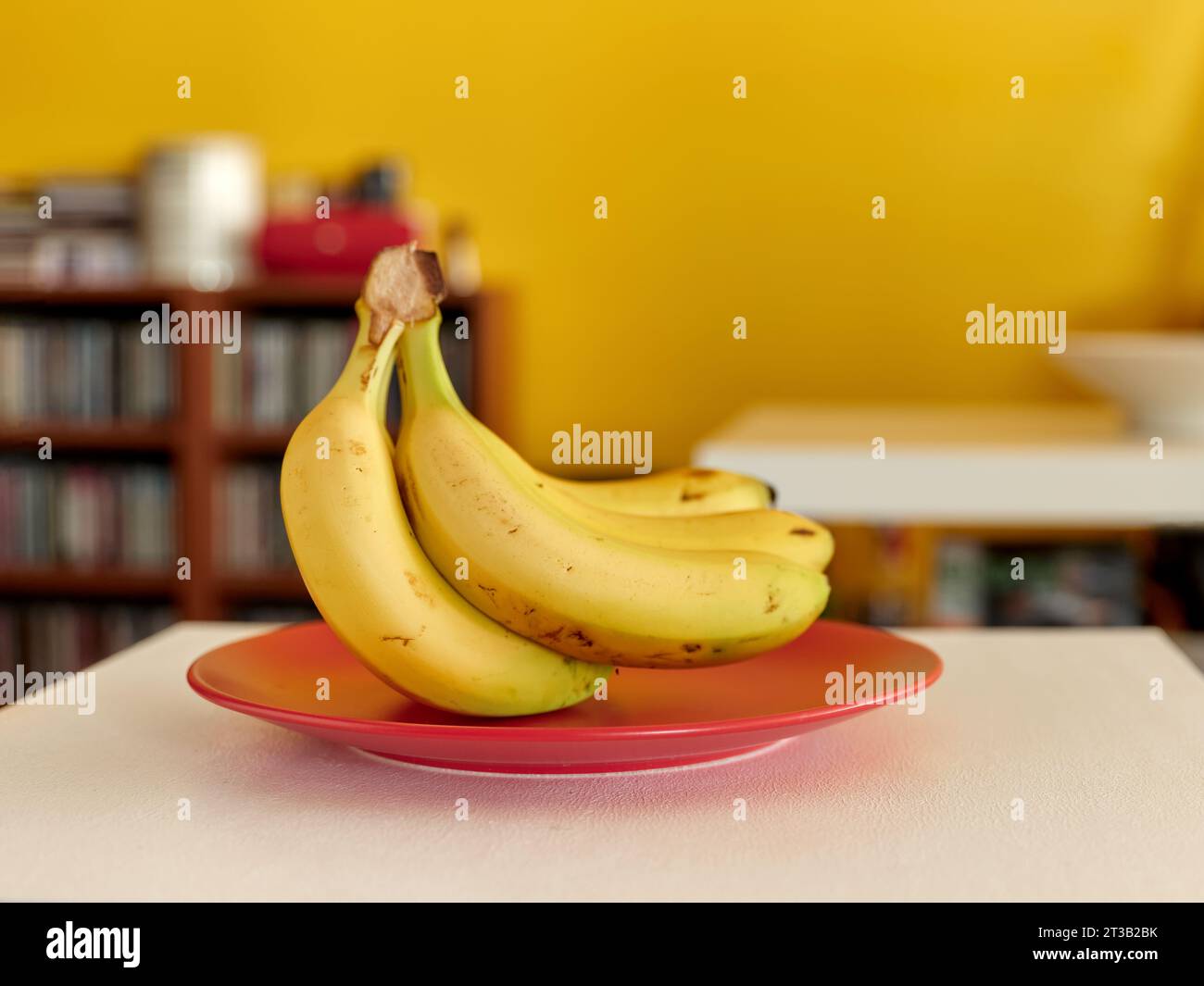 Bunch of fresh bananas on a red plate on the table with home interior ...