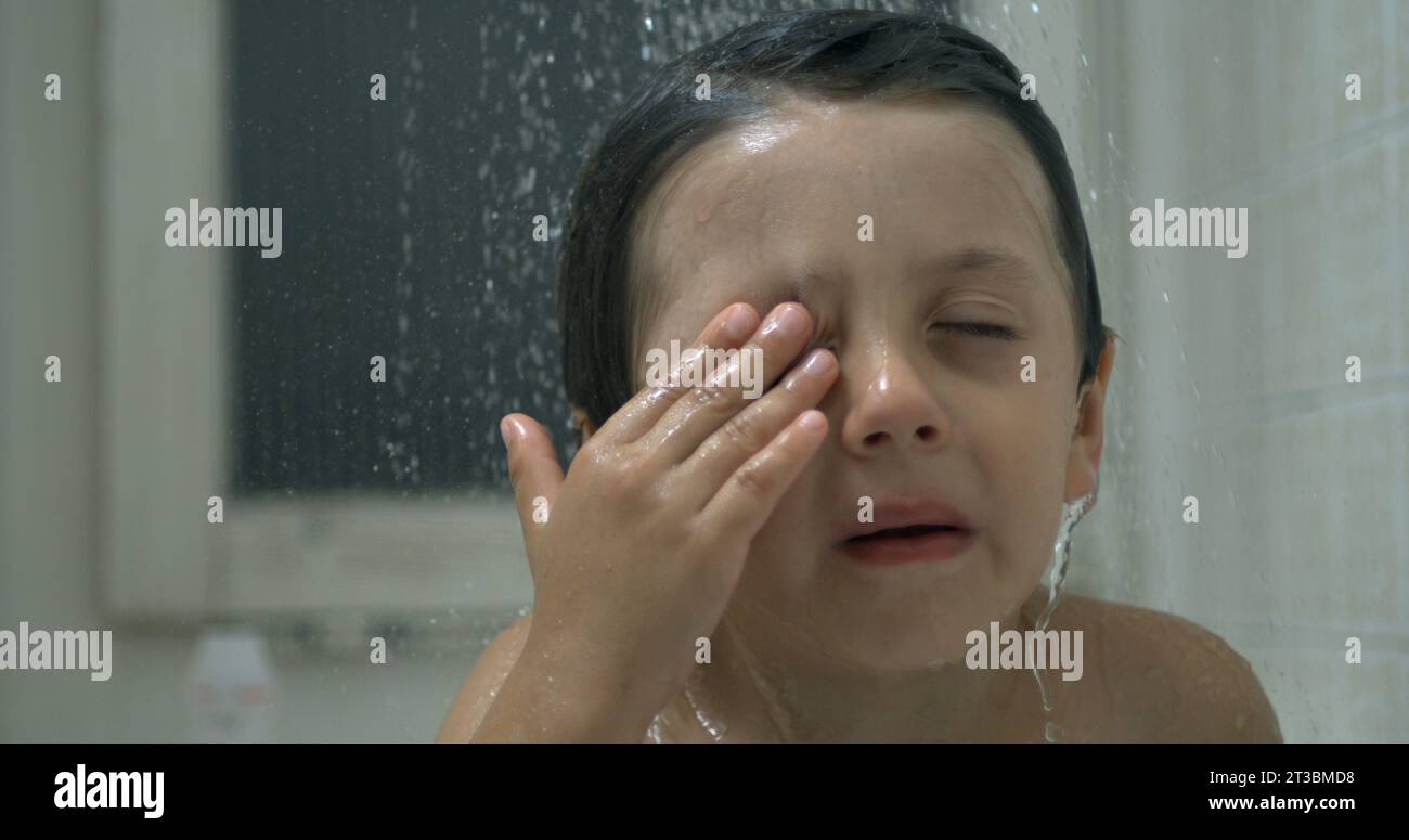 Child touching eye with finger while underneath of shower head with ...
