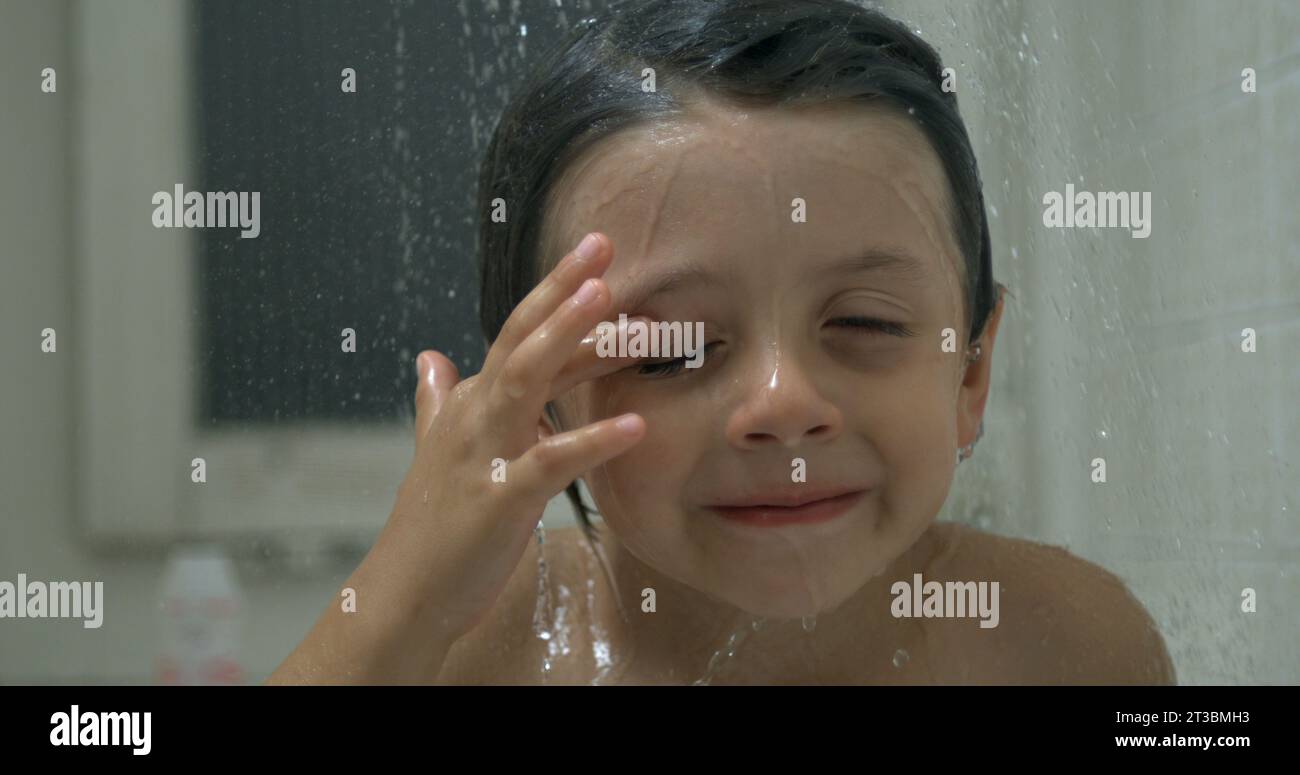 Close-up young boy's face underneath shower head with water pouring in ...