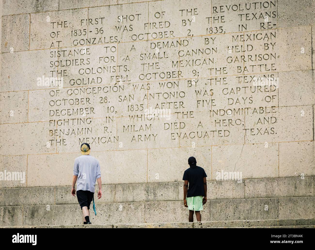 Two people standing together in front of a wall featuring a plaque ...