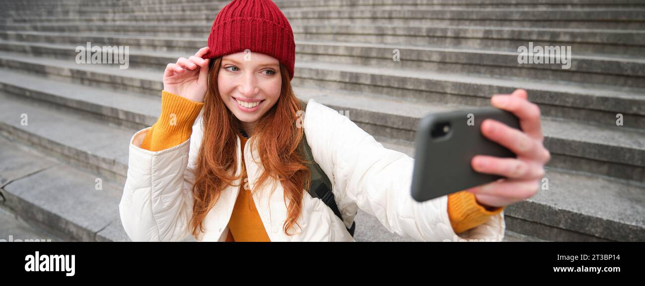 Stylish young girl in red hat, takes photos on smartphone camera, makes ...