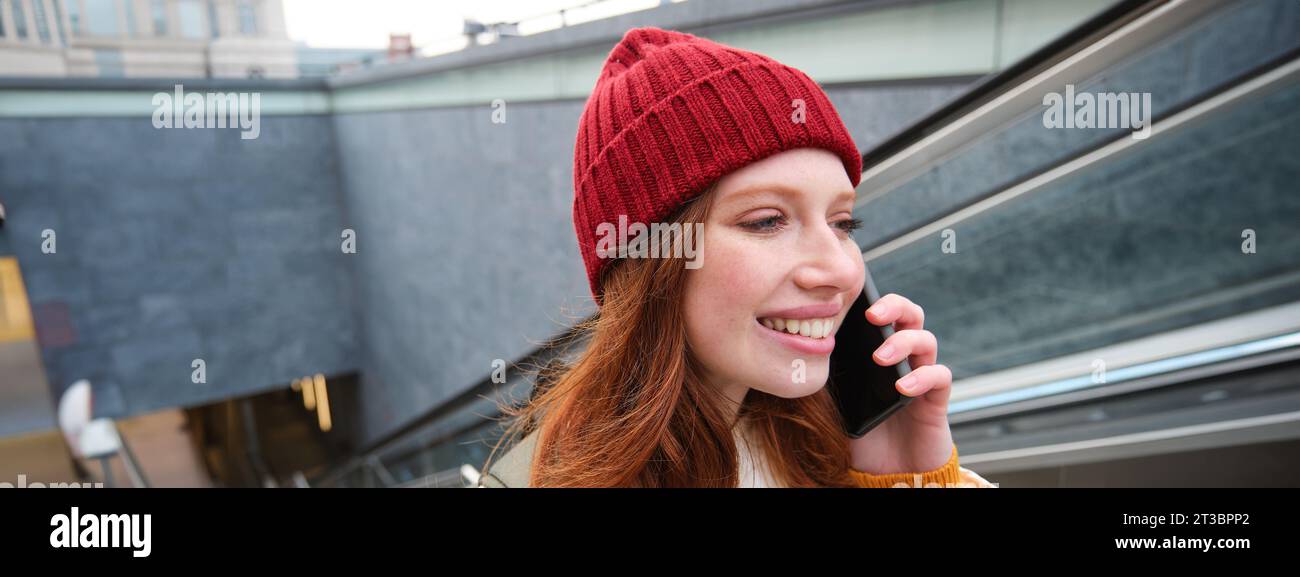 Portrait of happy redhead woman walking around town with smartphone ...