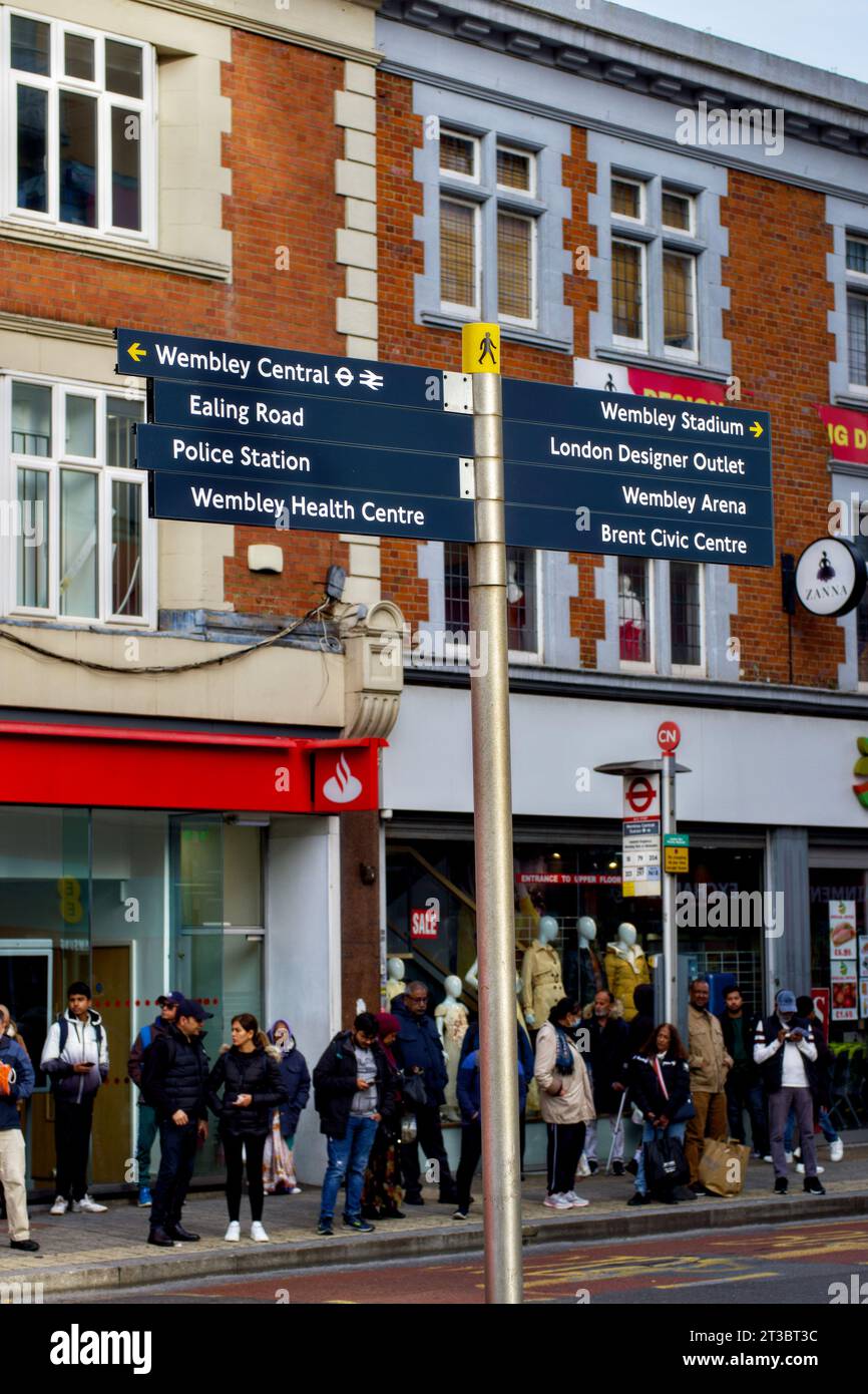 People waiting at bus stop behind direction sign, High Road, Wembley ...