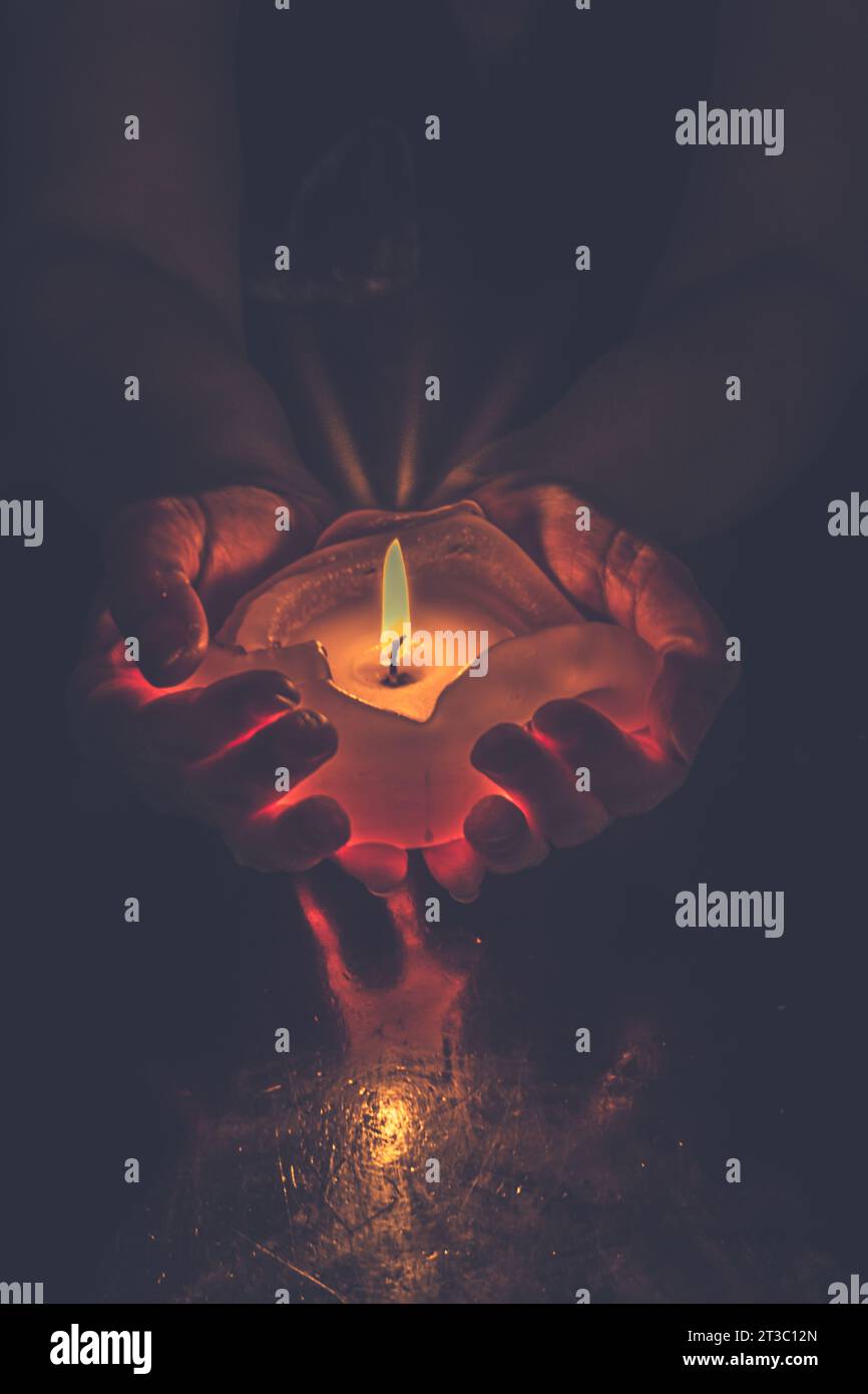 hands holding one burning candle with reflection against black ...