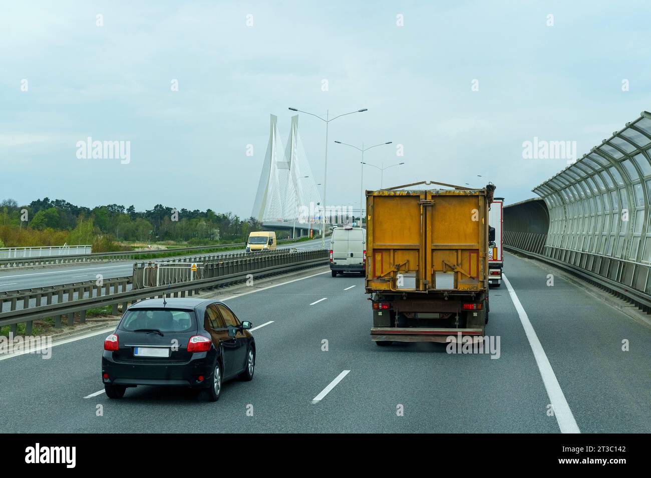 Trucks and cars are driving along the highway, there is a bridge ahead ...