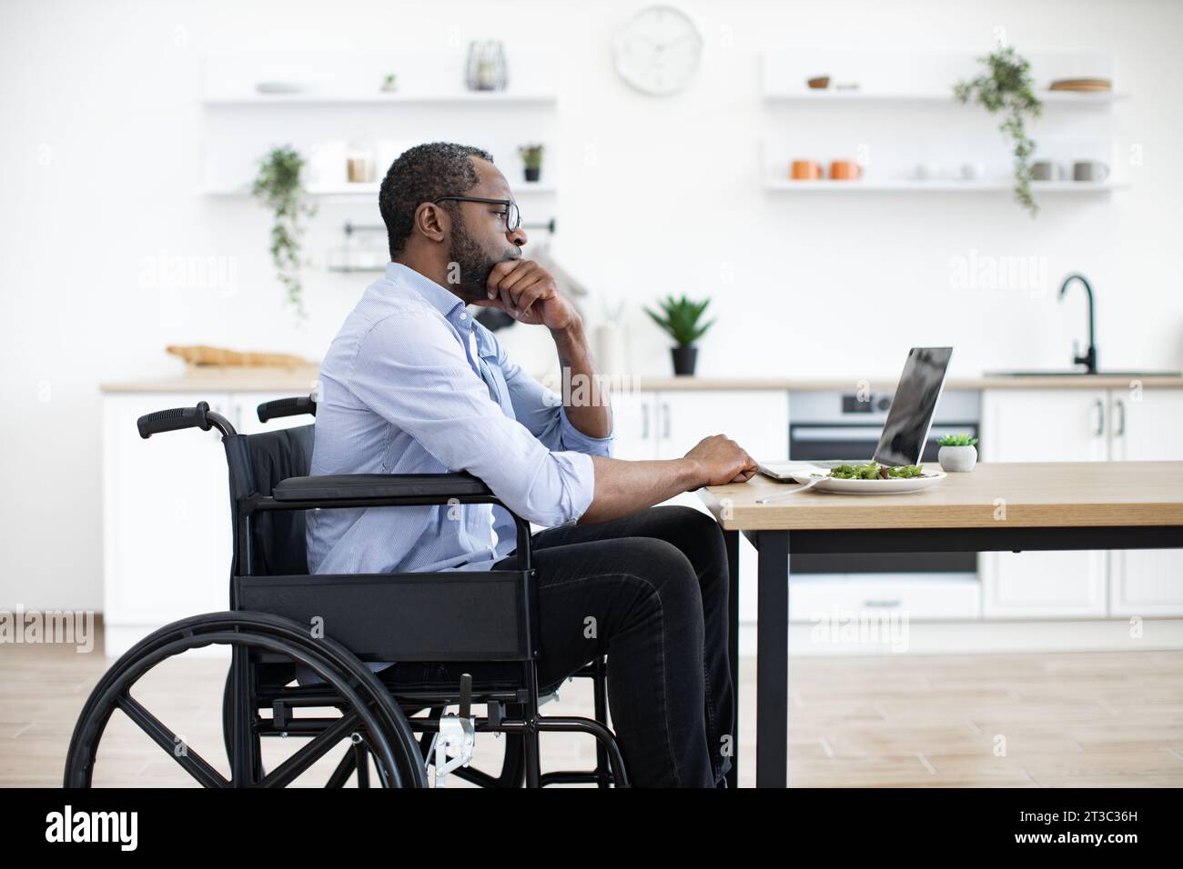 Wheelchair user typing on computer in kitchen interior Stock Photo - Alamy