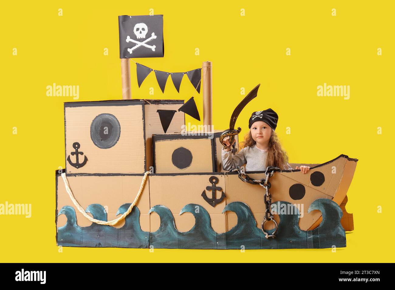 Cute little girl dressed as pirate playing with sword in cardboard ship ...