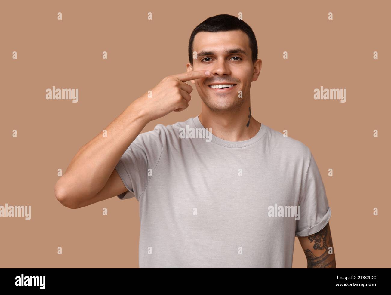 Ill young man pointing at nose on brown background Stock Photo - Alamy