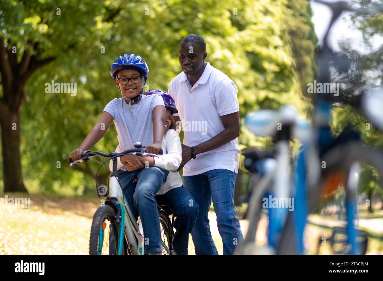 Father teaching his kids riding a bike and looking happy Stock Photo ...