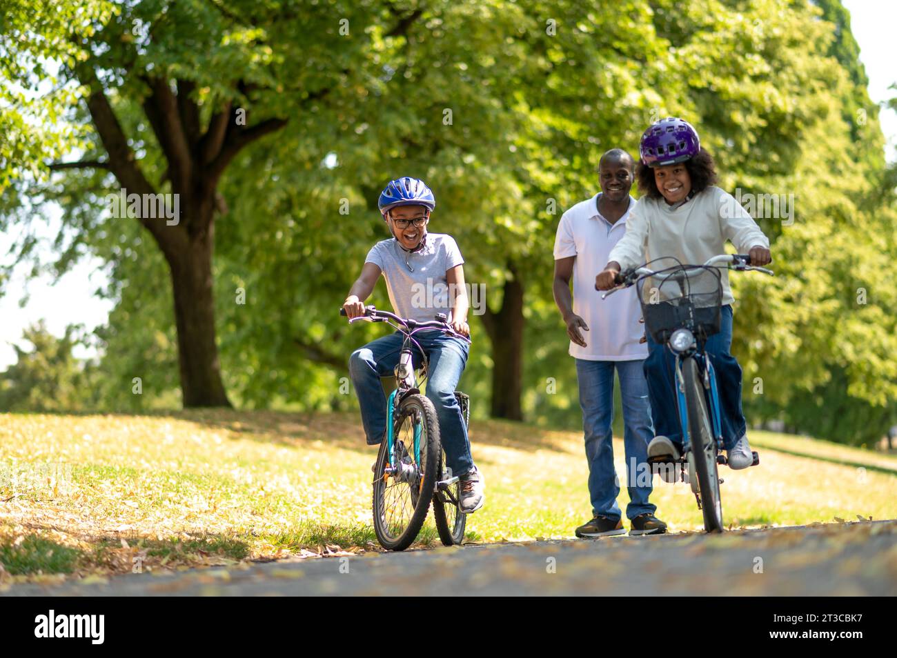 Father teaching his kids riding a bike and looking happy Stock Photo ...