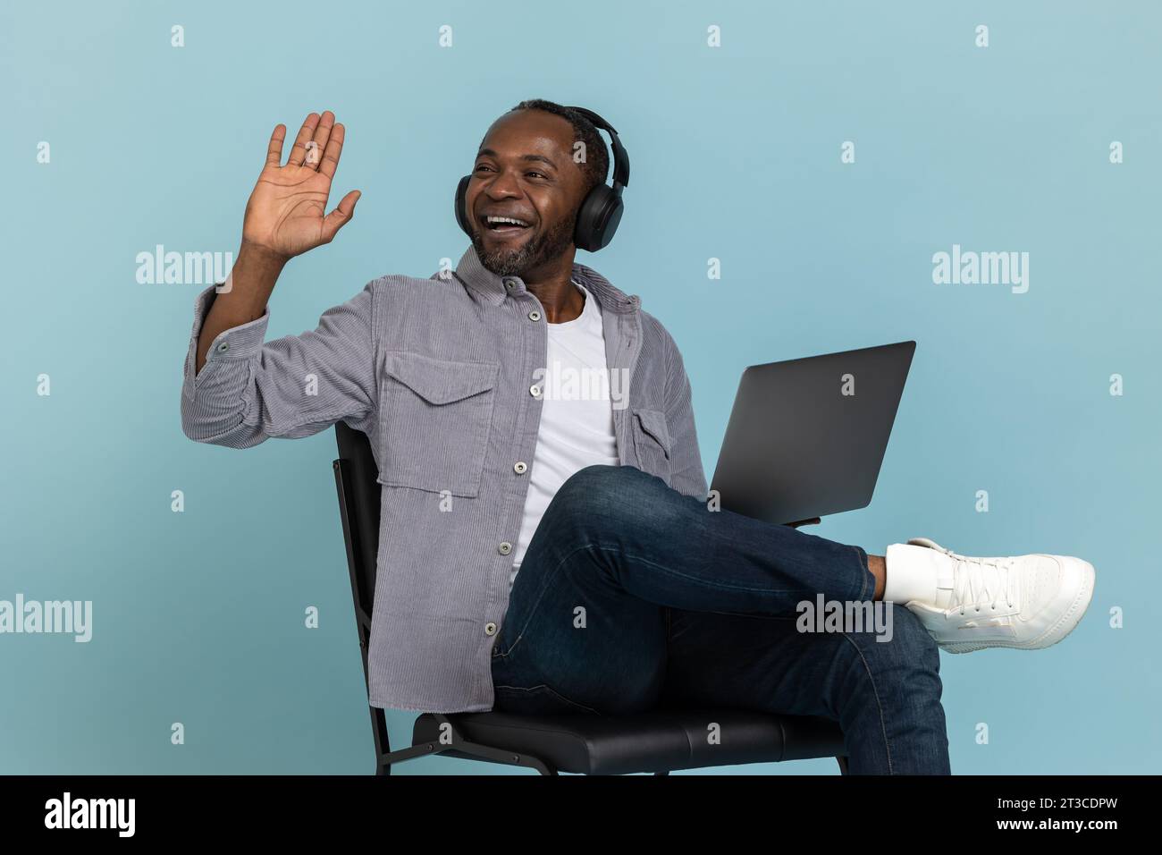 Excited black man with headphones using laptop looking away waving hand ...