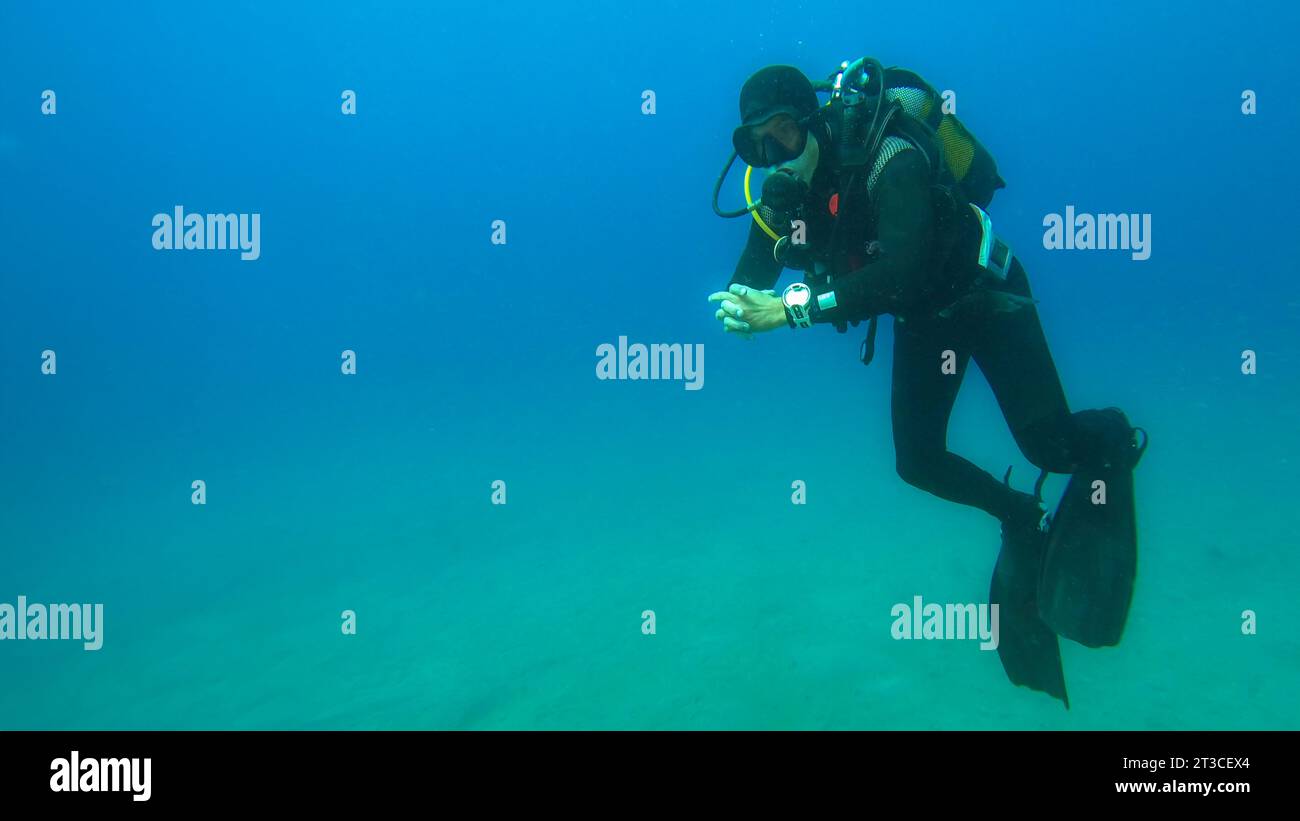 Male diver standing alone standing underwater, hands clasped surrounded ...